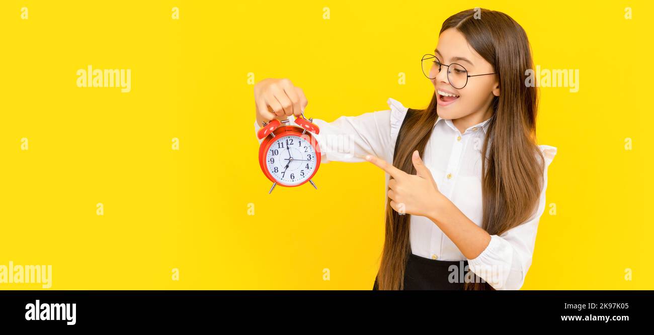 surprised kid in school uniform and glasses point finger on alarm clock ...