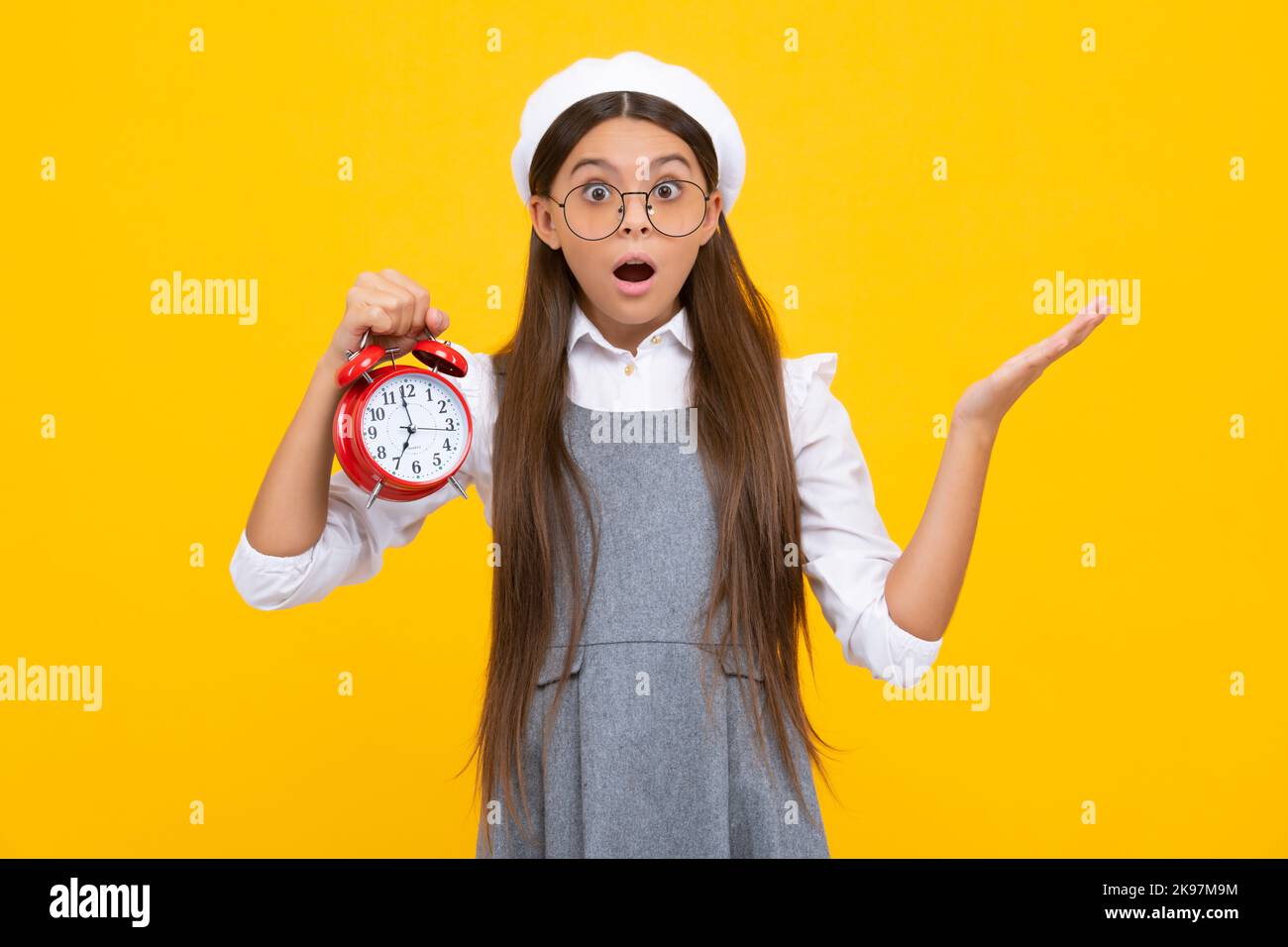 Child student girl with clock isolated on yellow background. Child back ...