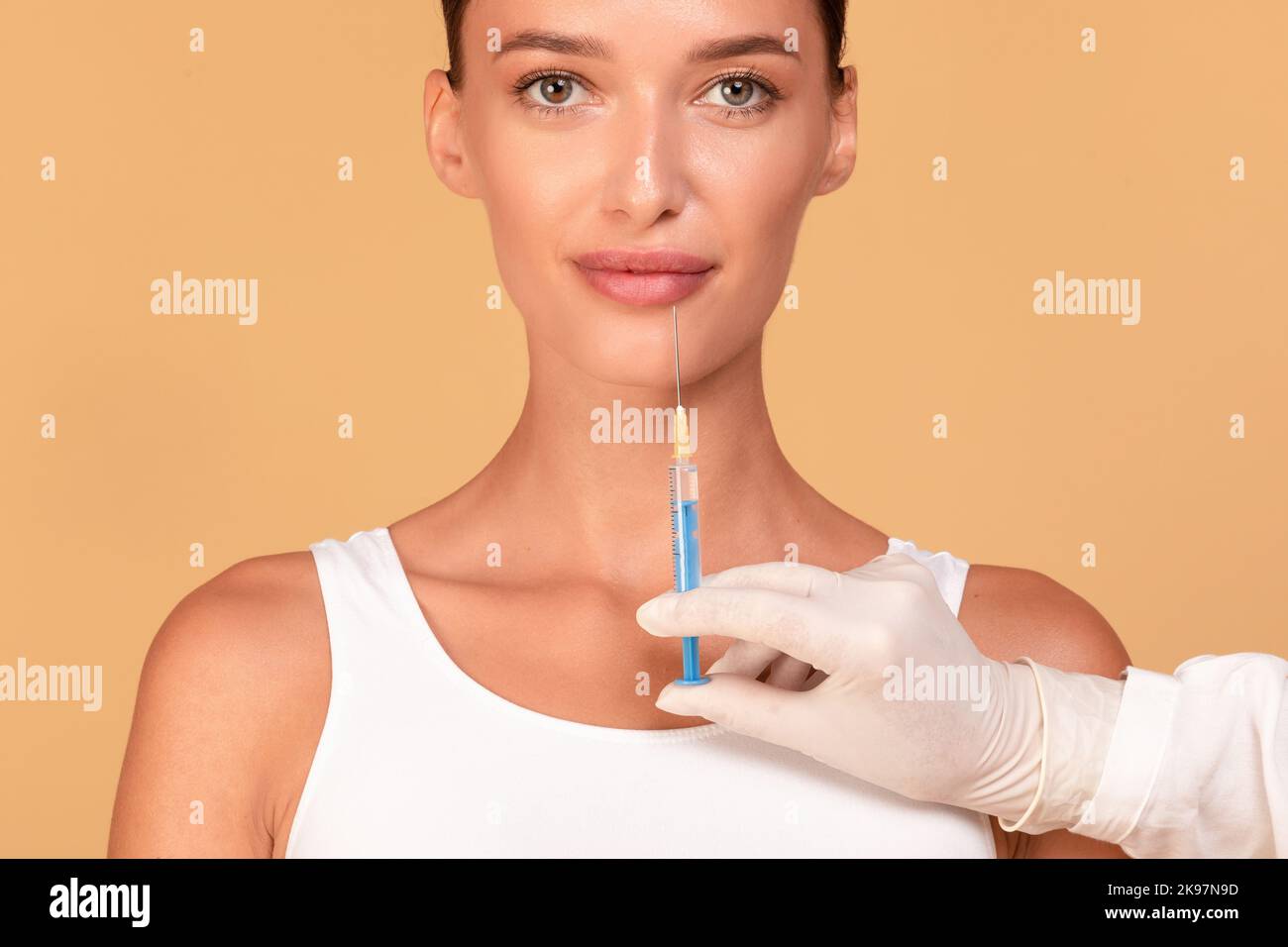 Beautiful young woman getting facial injection over beige background ...