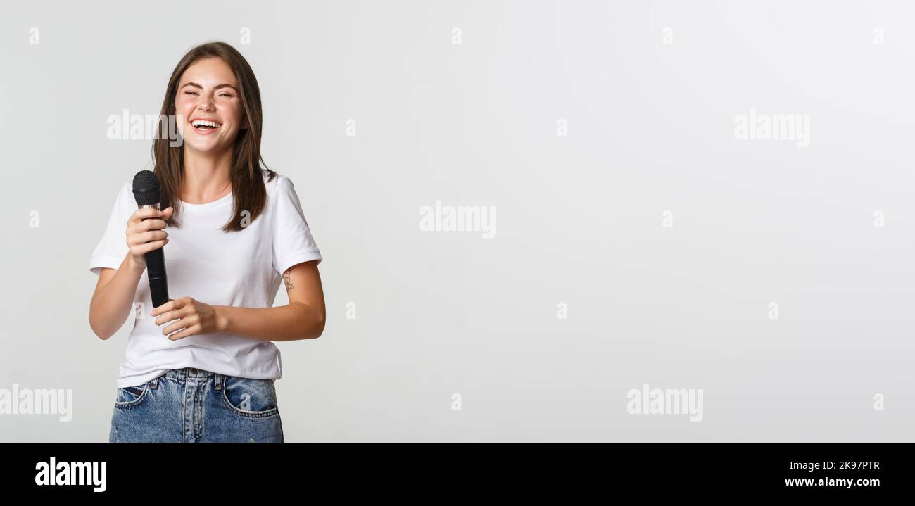 Happy laughing girl holding microphone and singing karaoke, white ...