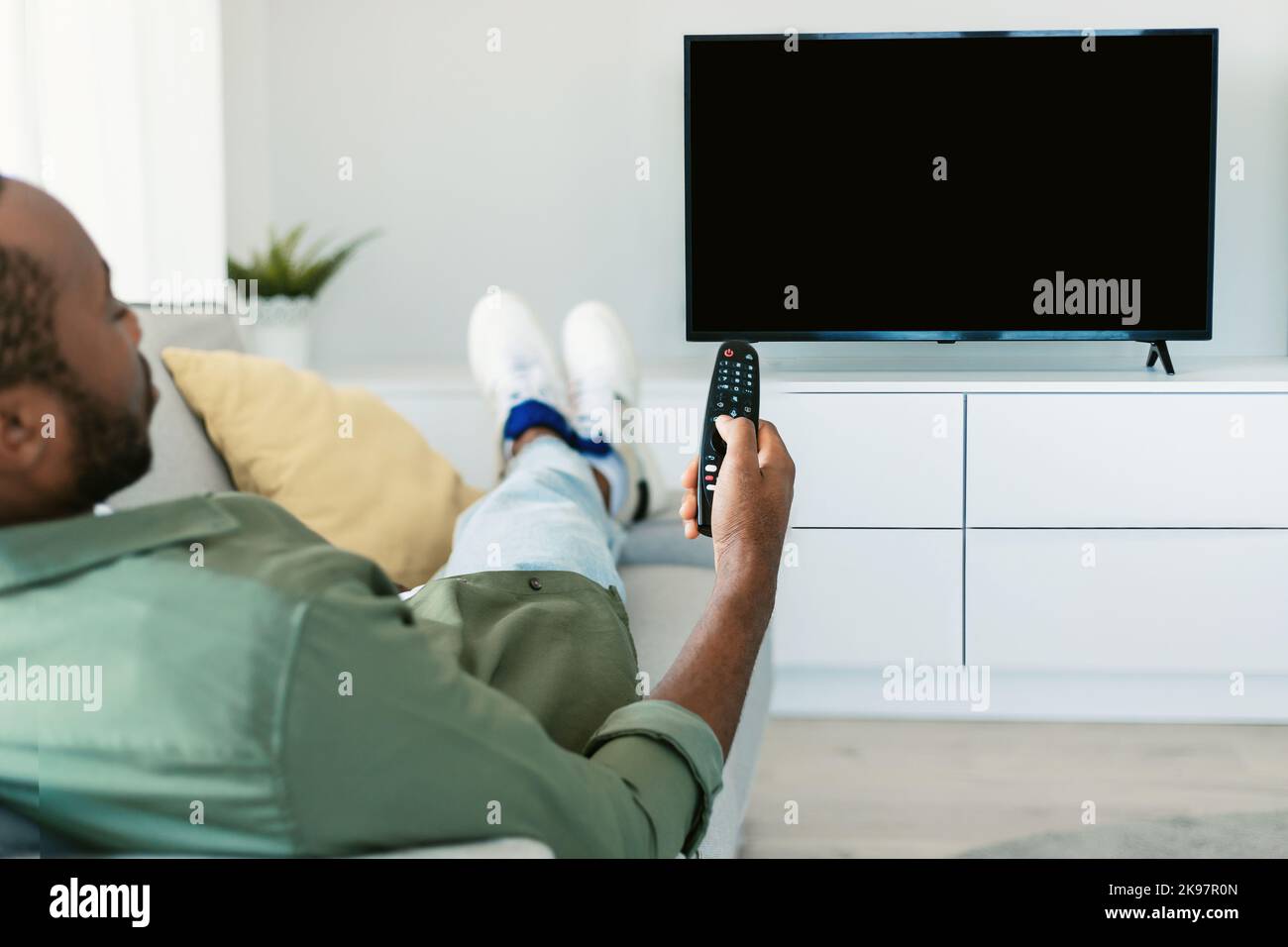 Back view of black man watching TV pointing remote control at empty ...