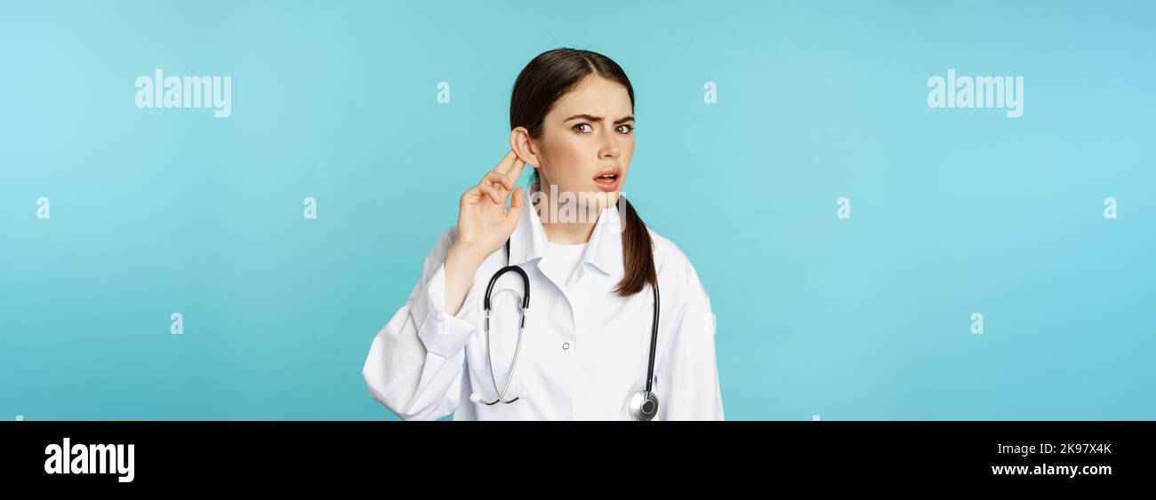 Image of confused woman doctor cant hear you, holding hand near ear and ...