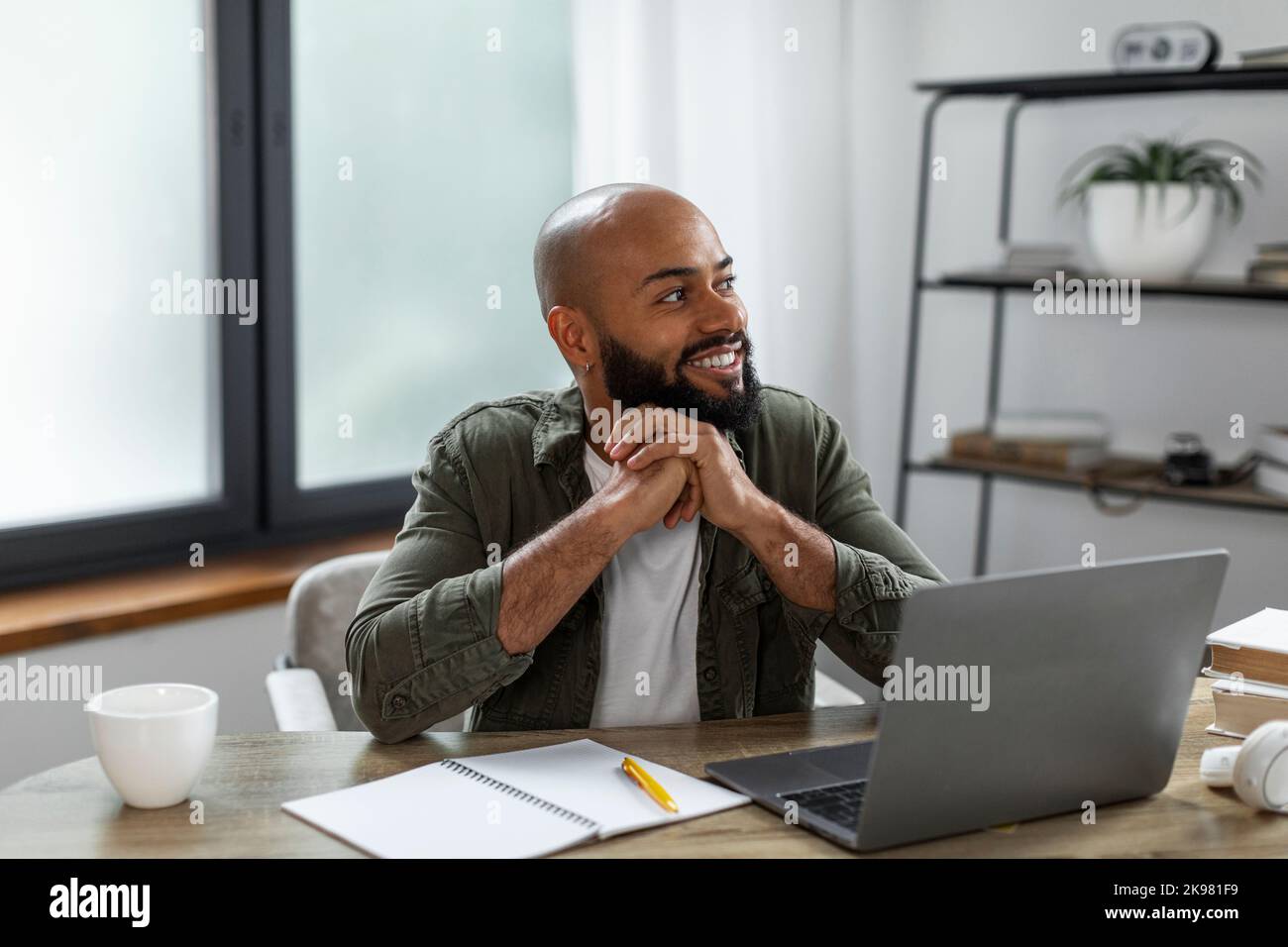 Happy latino man sitting at table in front of laptop computer at home ...