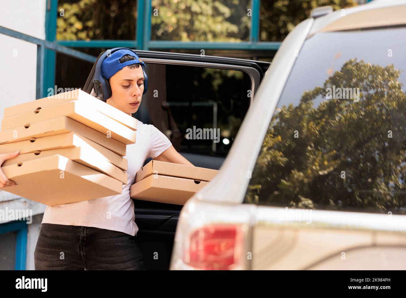 Courier carrying pizza to office by car, young woman holding boxes pile ...