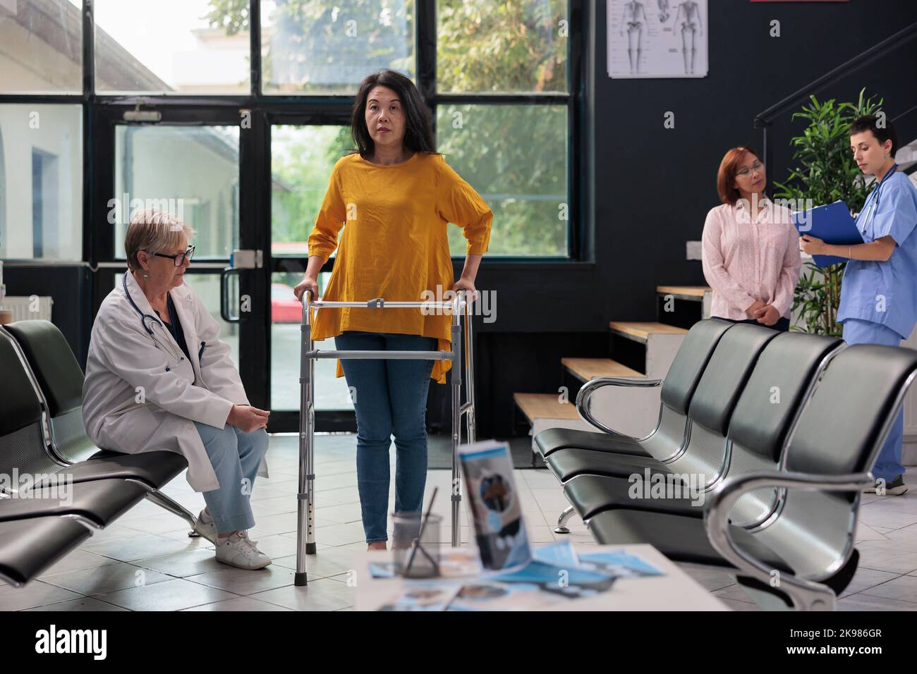 Senior doctor helping injured woman with leg fracture to recover from accident, using walking ...