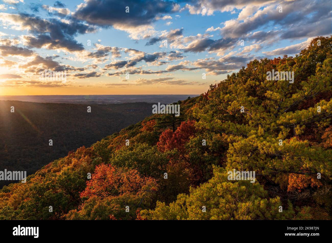 Sun setting behind clouds illuminating the fall colors of the trees in ...