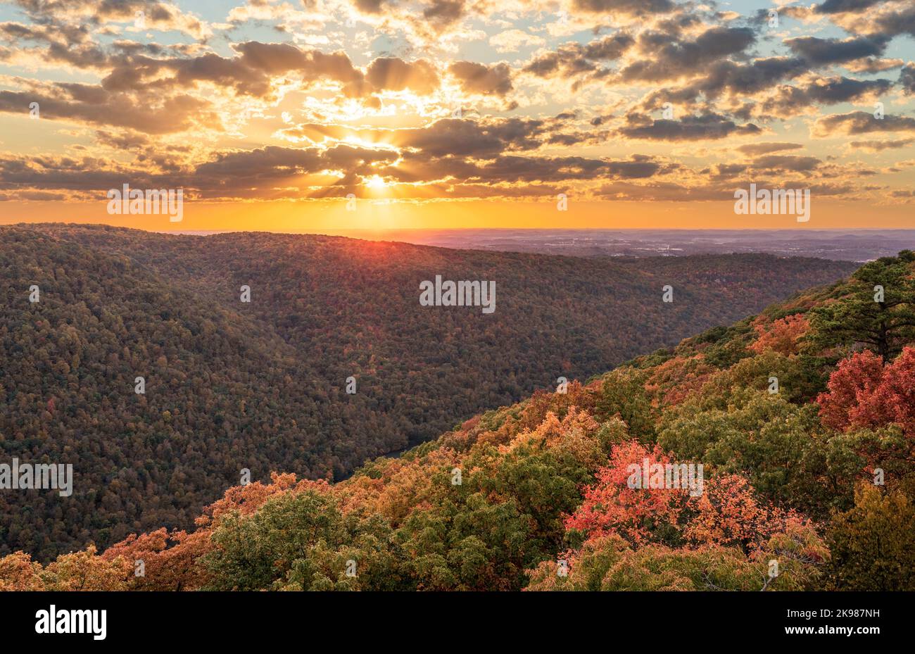 Sun setting behind clouds illuminating the fall colors of the trees in ...