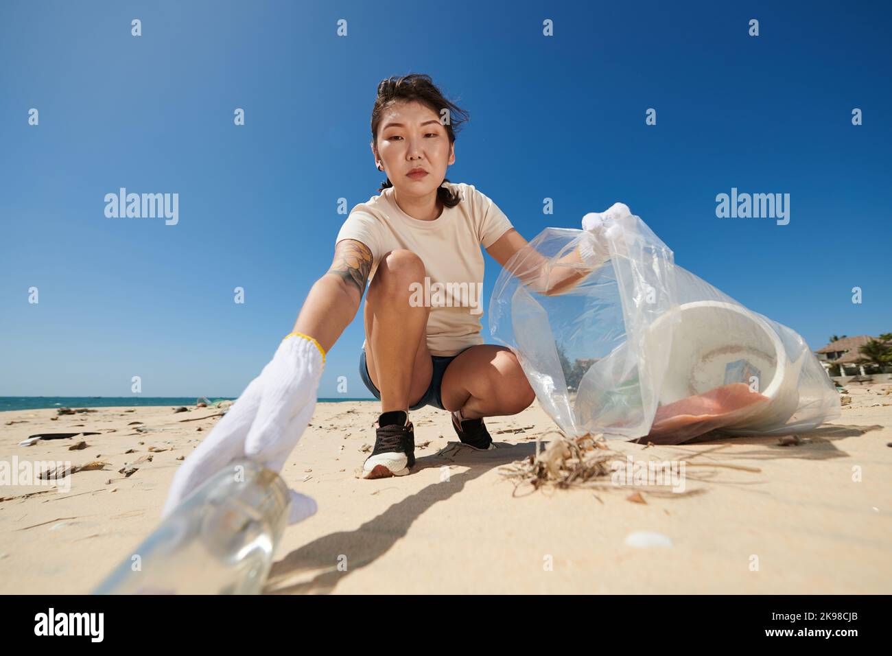 Serious female volunteer collecting garbage on sandy beach Stock Photo ...