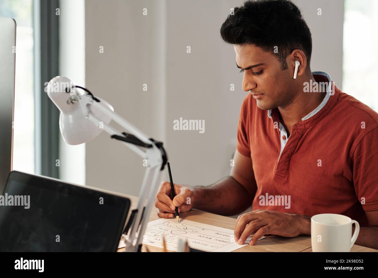Serious Indian software developer listening to music in earbuds when drawing wireframe before ...