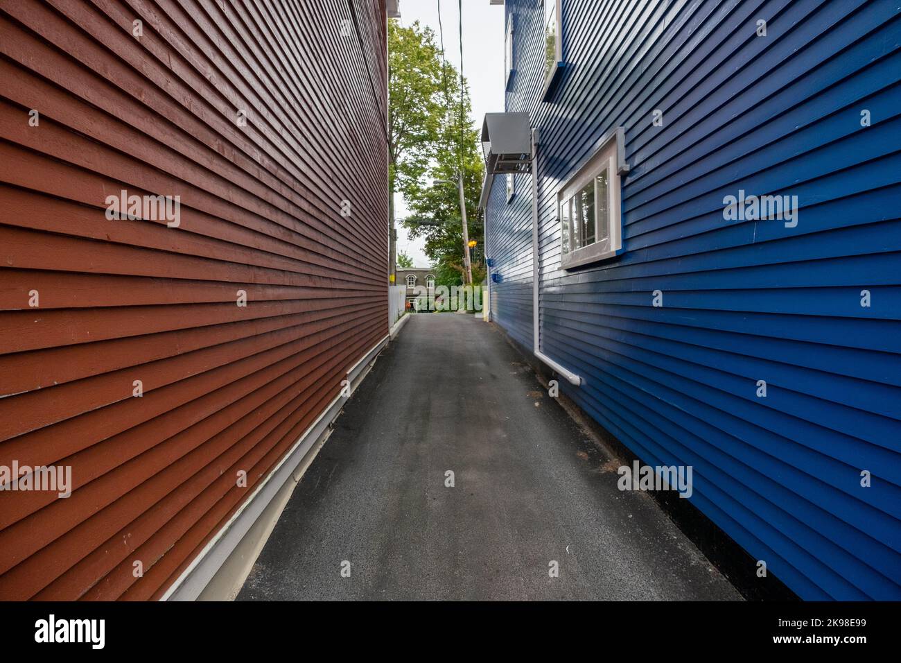 A narrow paved alleyway with a vibrant red wooden house wall and a ...