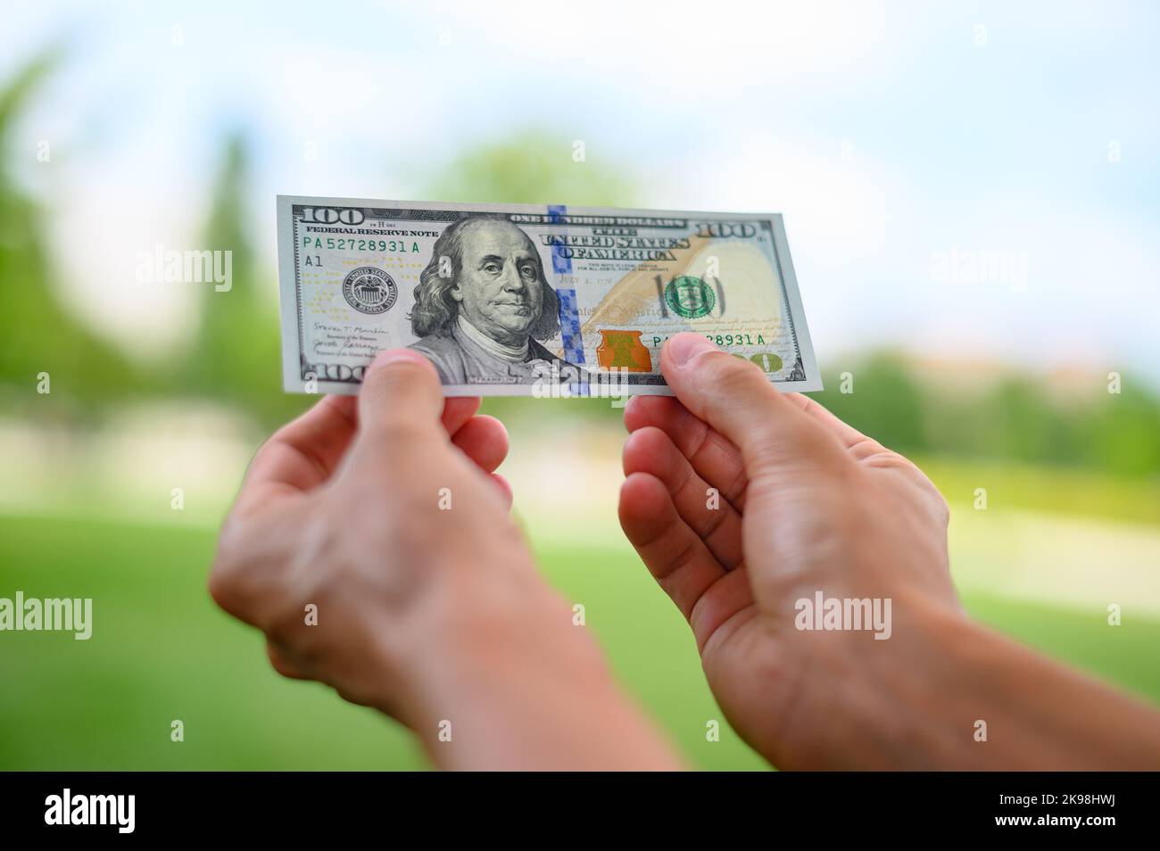 Close up 100 Dollar bank note in hand on grass background. One hundred ...