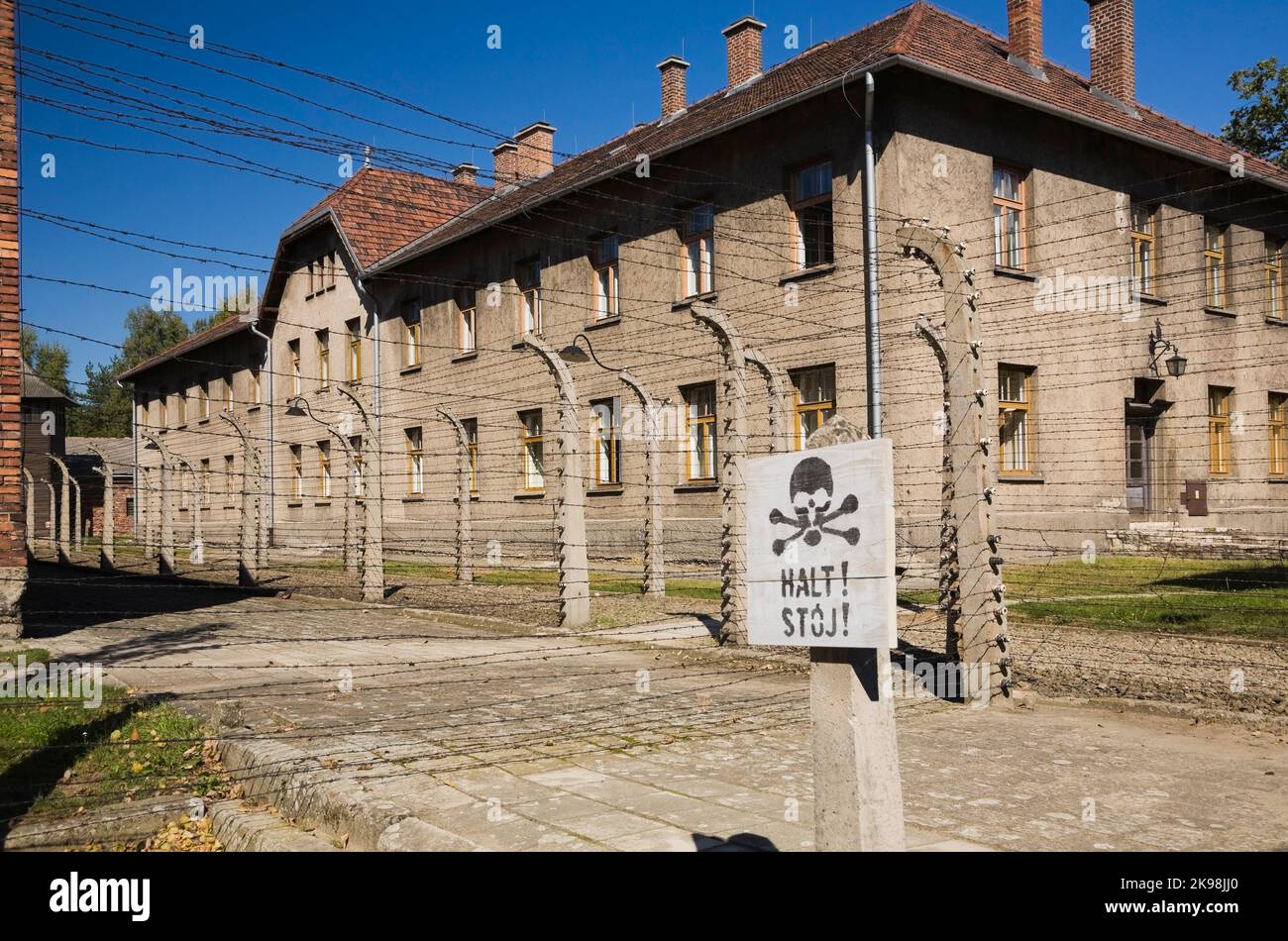 Stop warning sign in front of a electrified barbwire fence and building ...