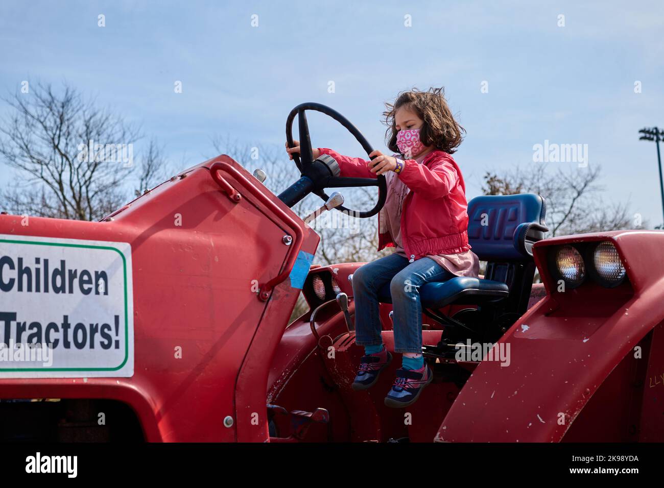 Girl in a mask pretending to drive a tractor at the county fair exhibit ...