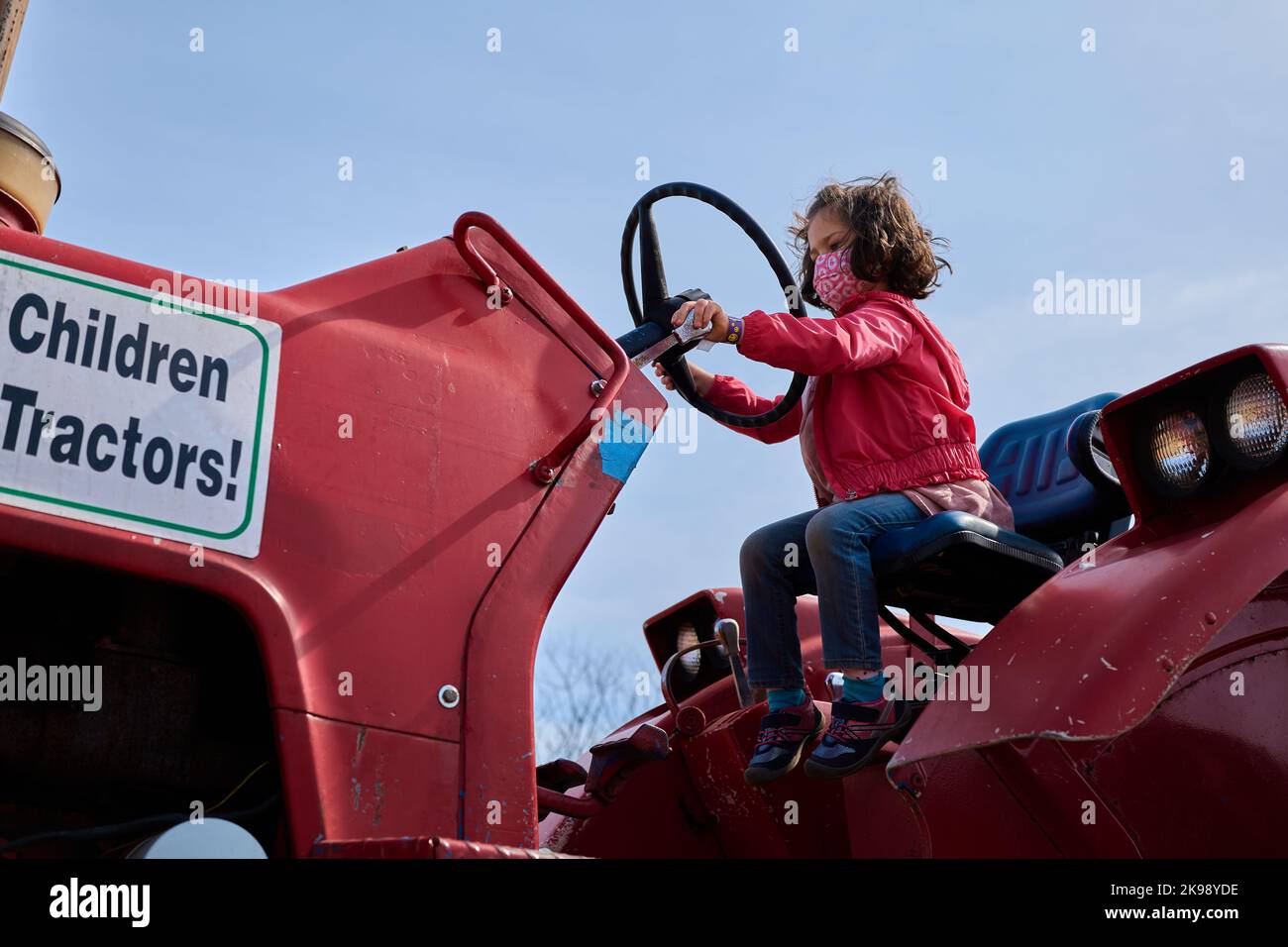 Girl in a mask pretending to drive a tractor at the county fair exhibit ...