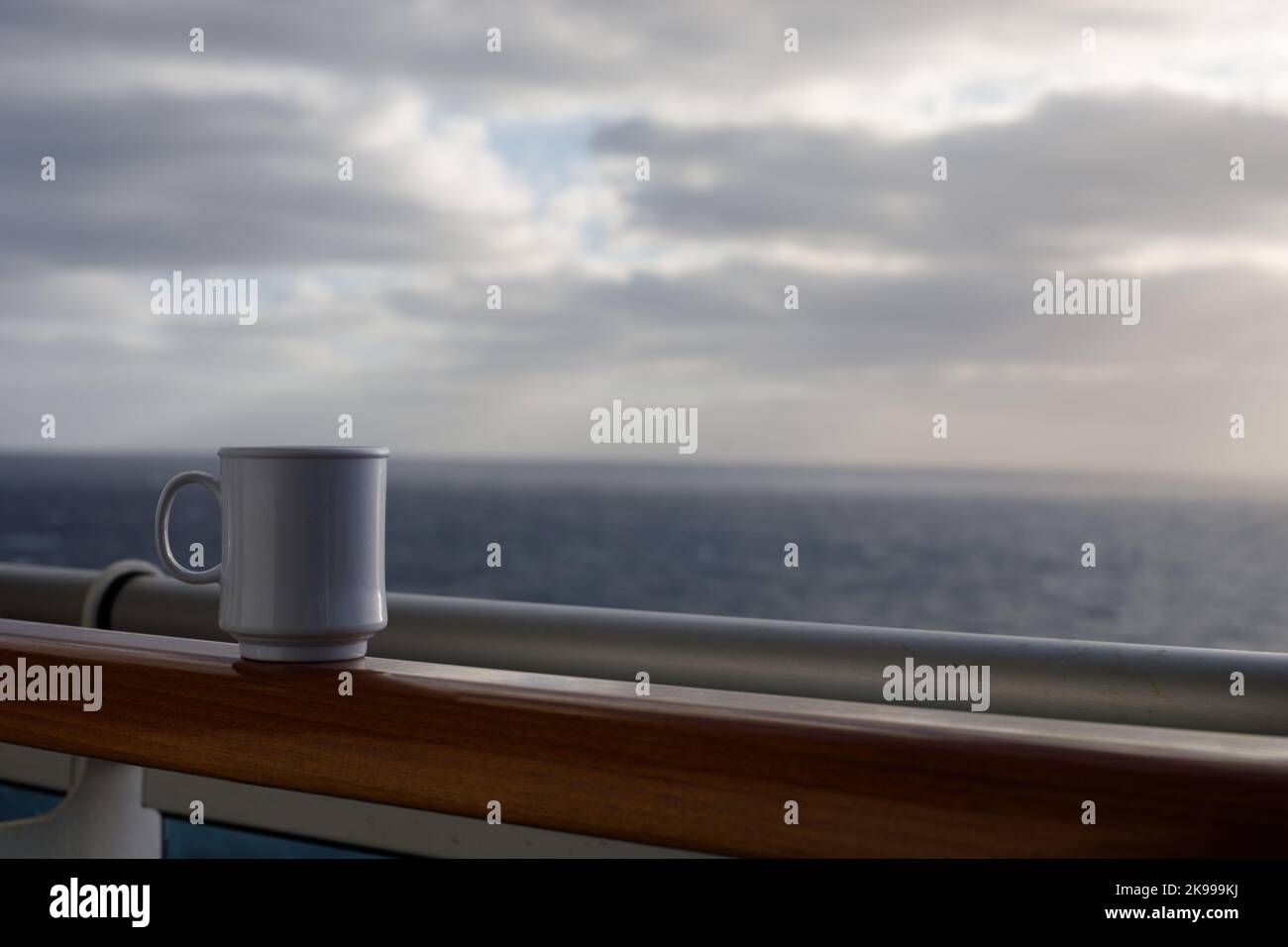cup of tea resting on the railing of a cruise ship with the ocean at ...