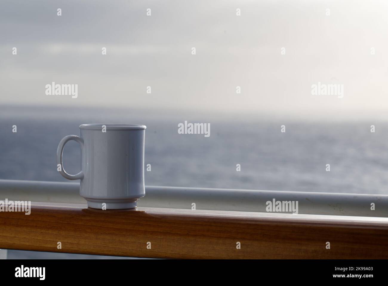 cup of tea resting on the railing of a cruise ship with the ocean at ...