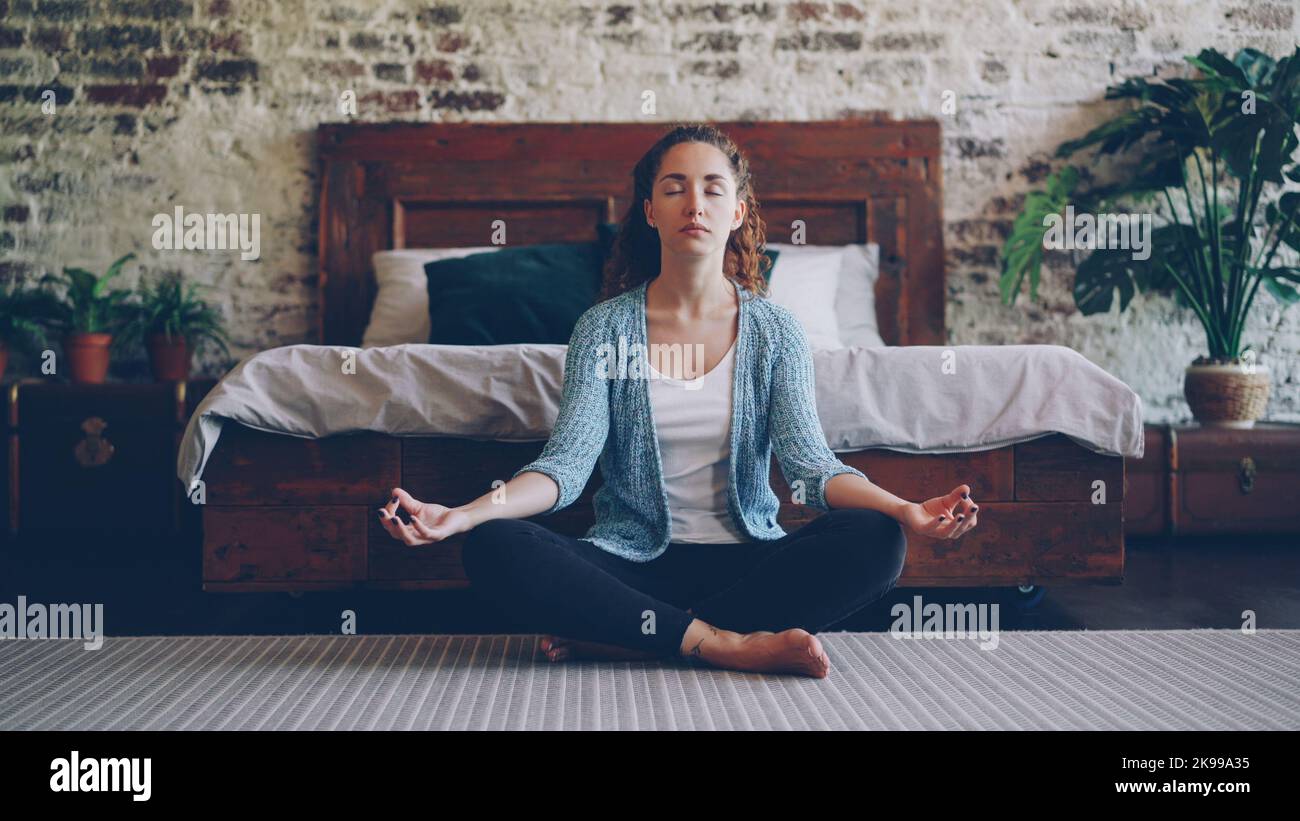 Beautiful young lady is sitting in lotus position on bedroom floor and ...