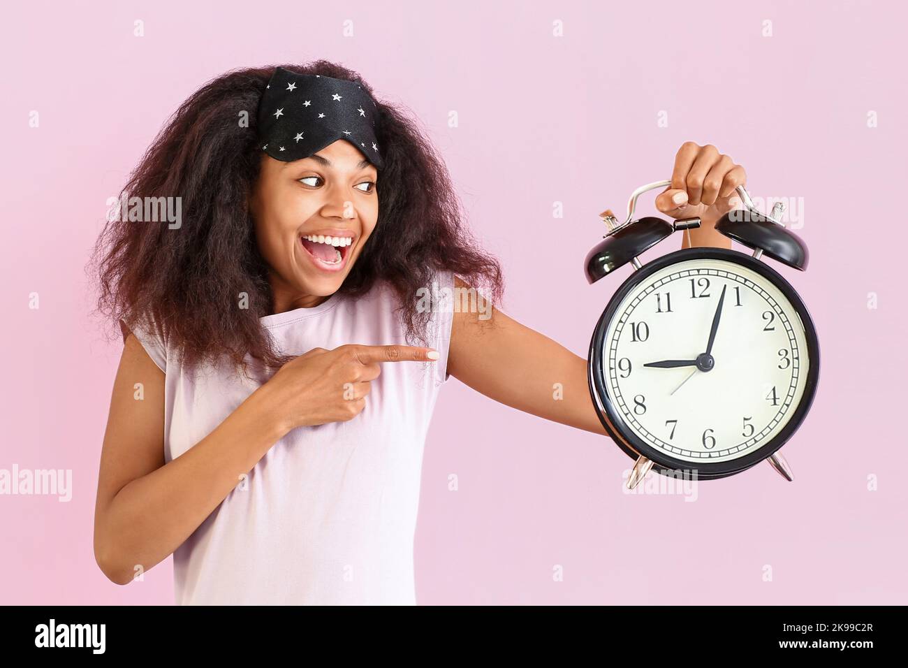 Happy African-American woman with sleep mask and big alarm clock on ...