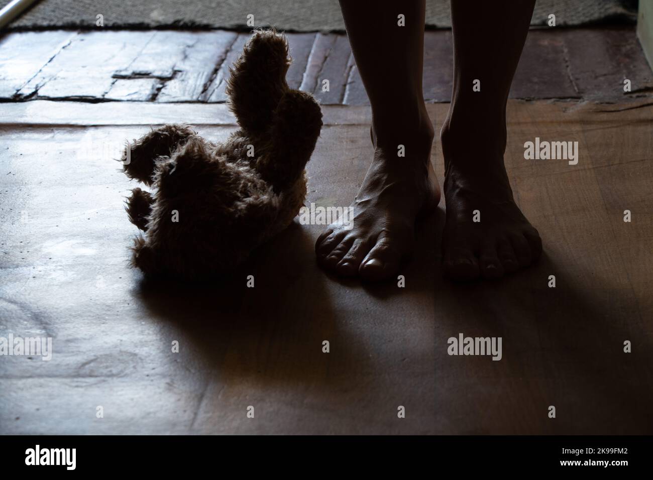 female feet next to a baby teddy bear on the floor in the dark in the ...