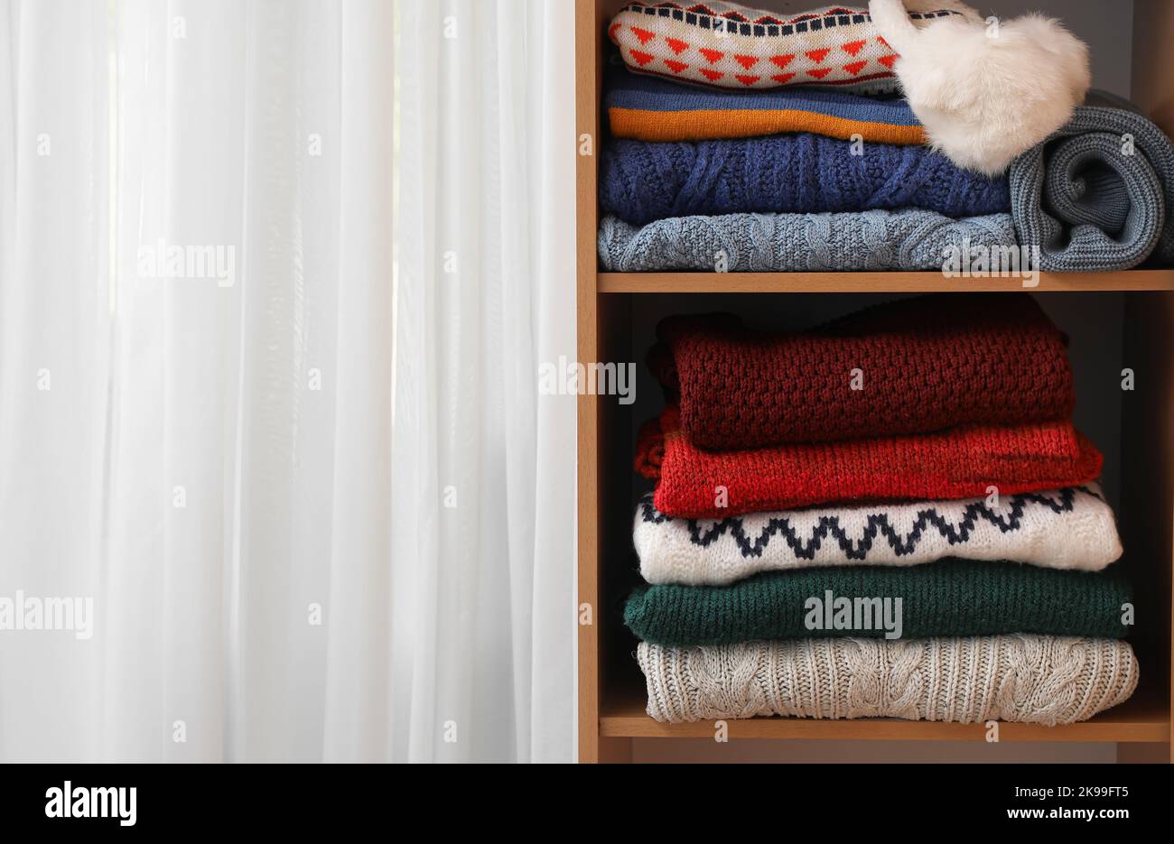 Shelving unit with folded sweaters near light curtain, closeup Stock ...