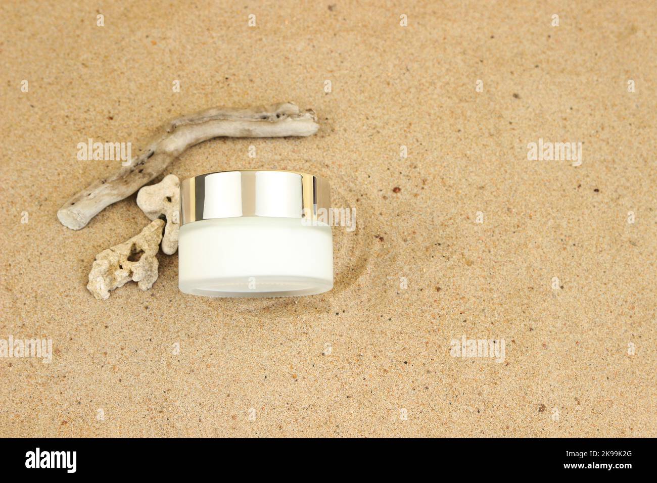 Cosmetic glass jar with white moisturizer and metal cap on beach sand ...