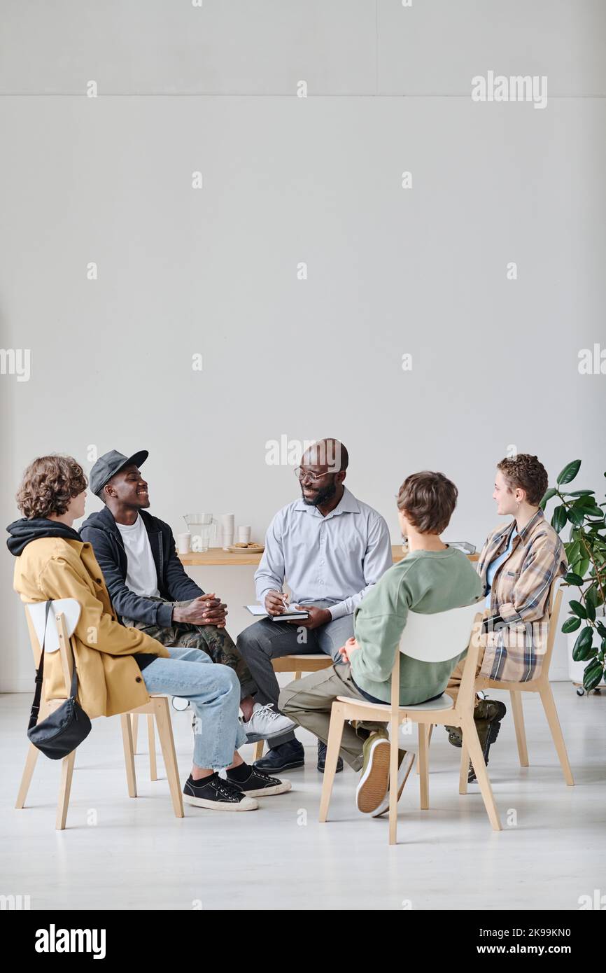 Group of students sitting on chairs with coach and discussing ...