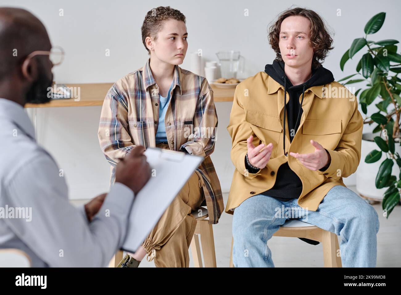 Teenage boy talking to therapist while he making notes during ...