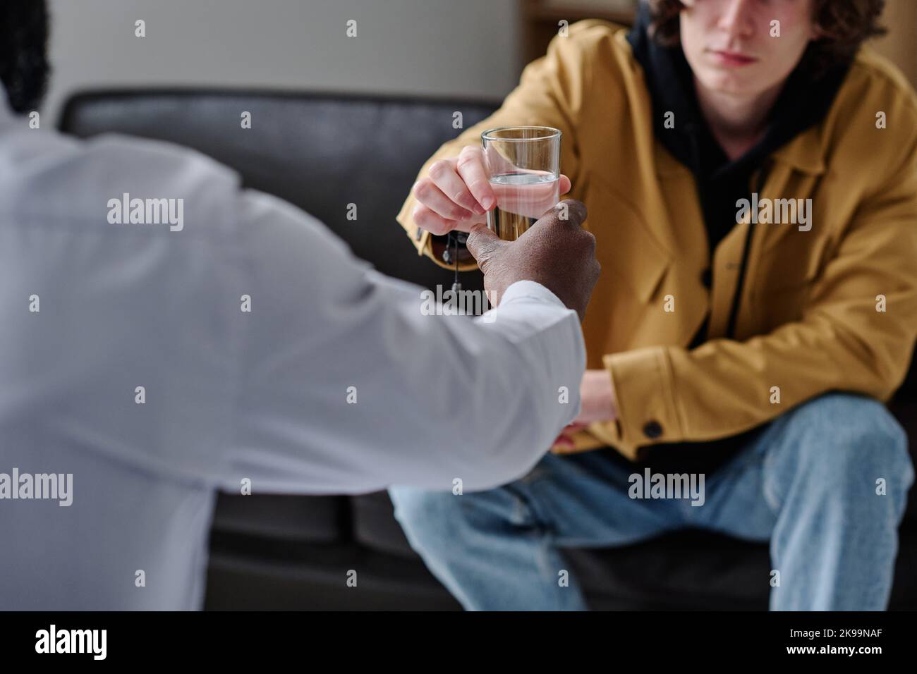 Close-up of teenage boy drinking water while talking to psychologist at ...