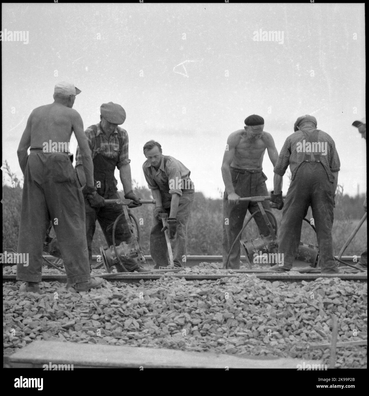 Track workers adjust the ballast under the tracks with vibrator skewers ...
