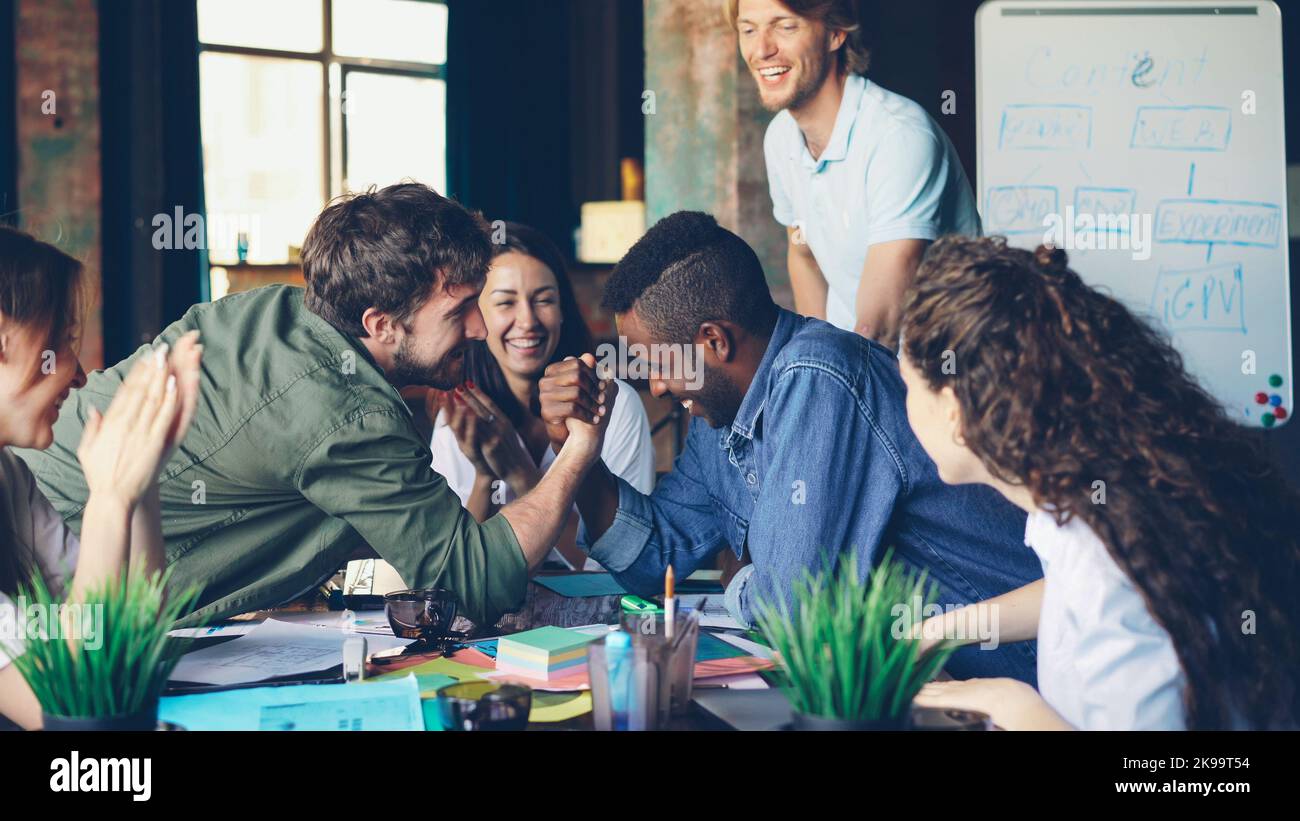 Cheerful coworkers multiethnic team are practicing arm wrestling during ...