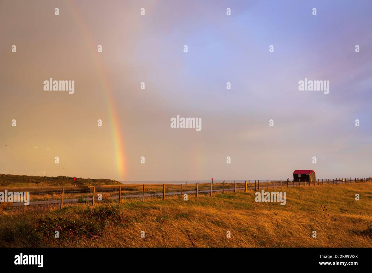 Rainbow after the storm at sunset over the red roofed hut Rye Harbour ...