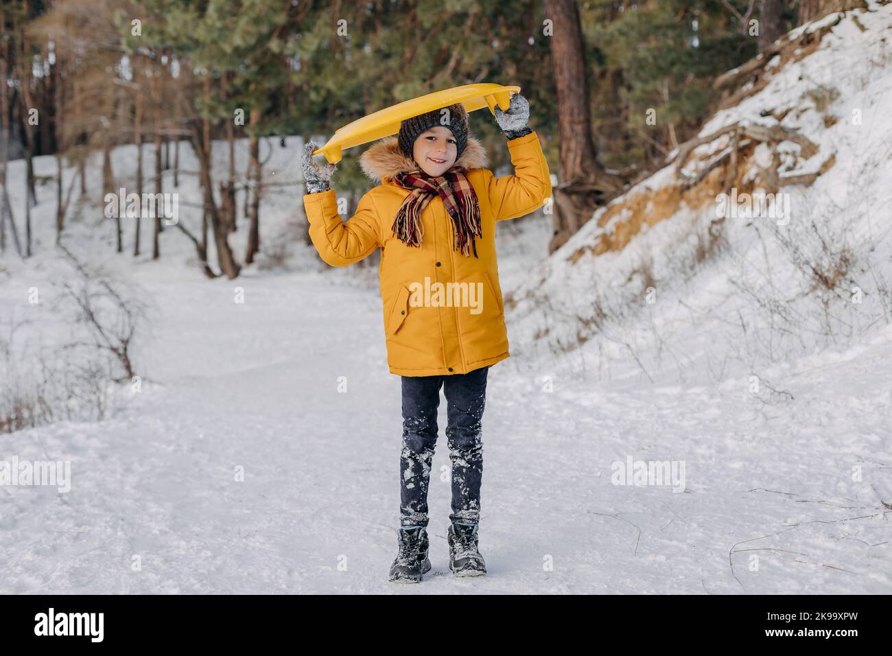 Happy fun kid holding a plastic sled on the background of snowy forest ...