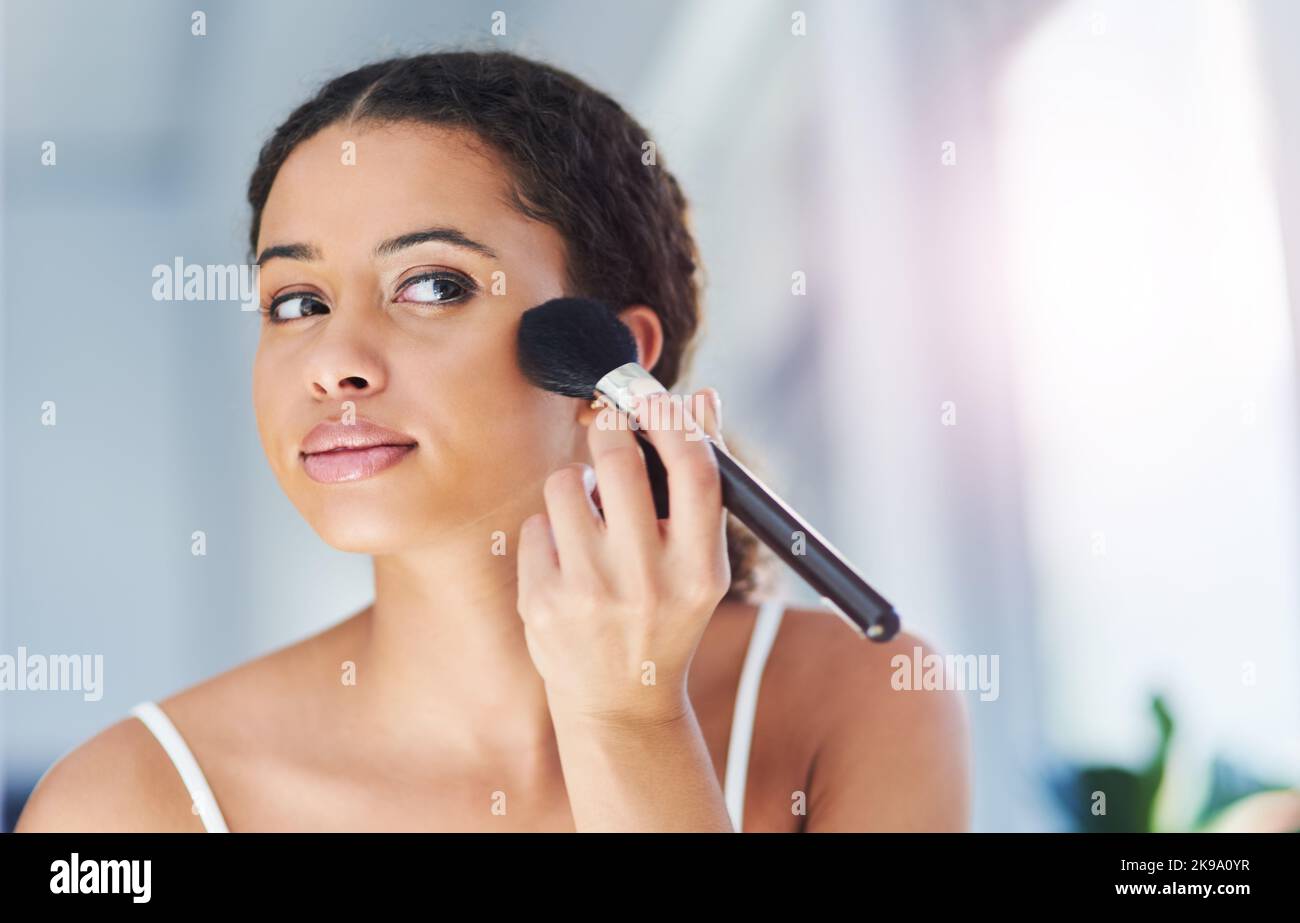 Getting ready for her date. a young woman applying makeup to her cheeks ...