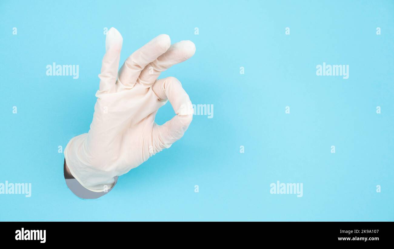 A female gloved hand sticks out through a blue paper background and ...