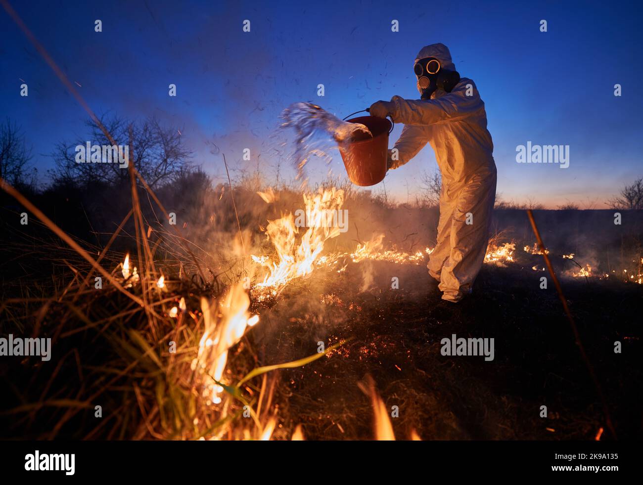 Fireman fighting fire in field with blue night sky on background. Man ...