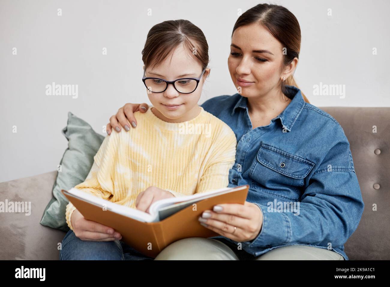 Portrait of teen girl with Down syndrome reading book with loving ...