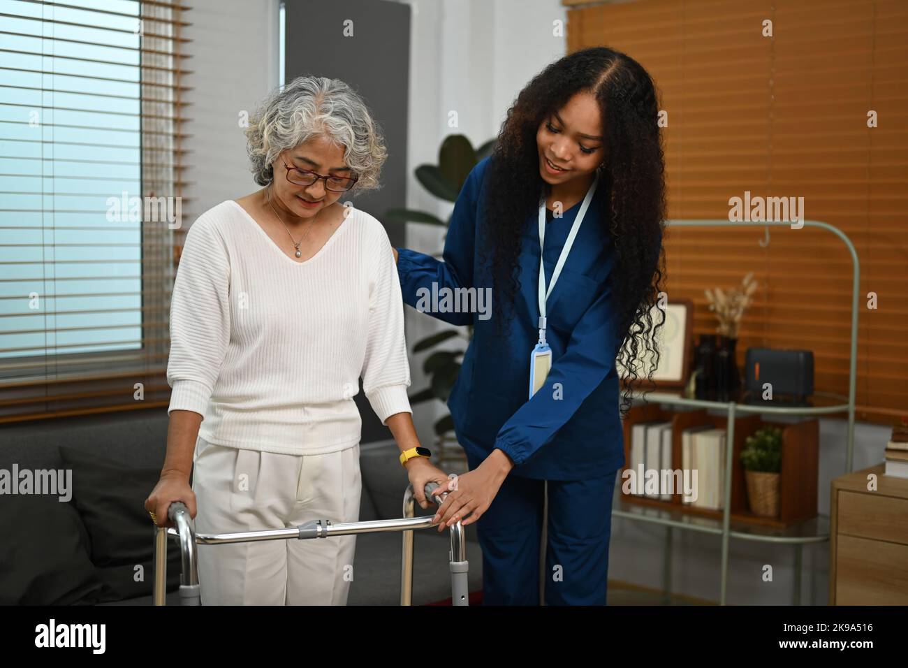 Young female caregiver is teaching senior woman to walk with walker ...