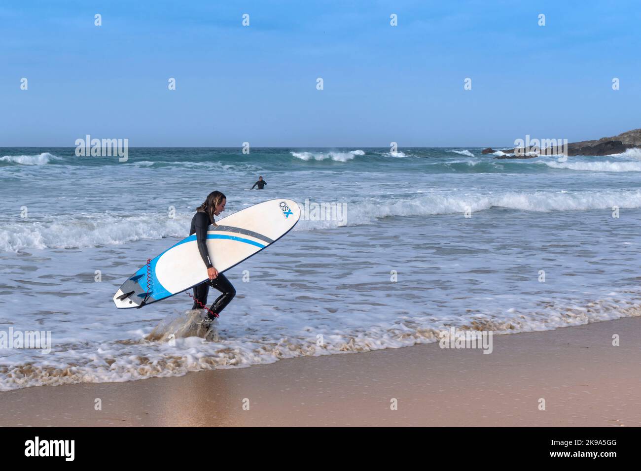 A tired surfer carrying a surfboard walking along the shoreline on ...