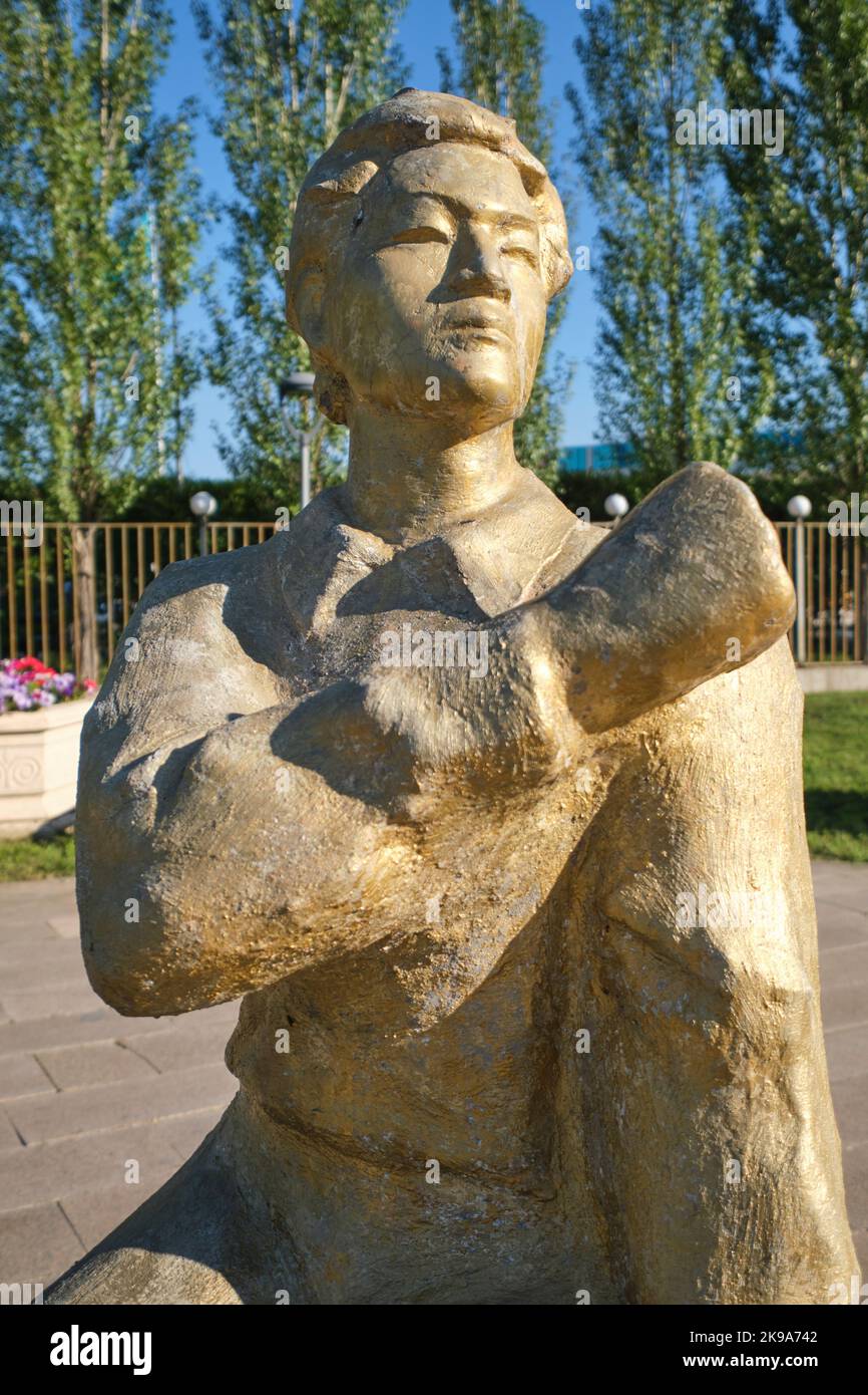 A gold painted statue, sculpture of a student, proudly sitting and ...