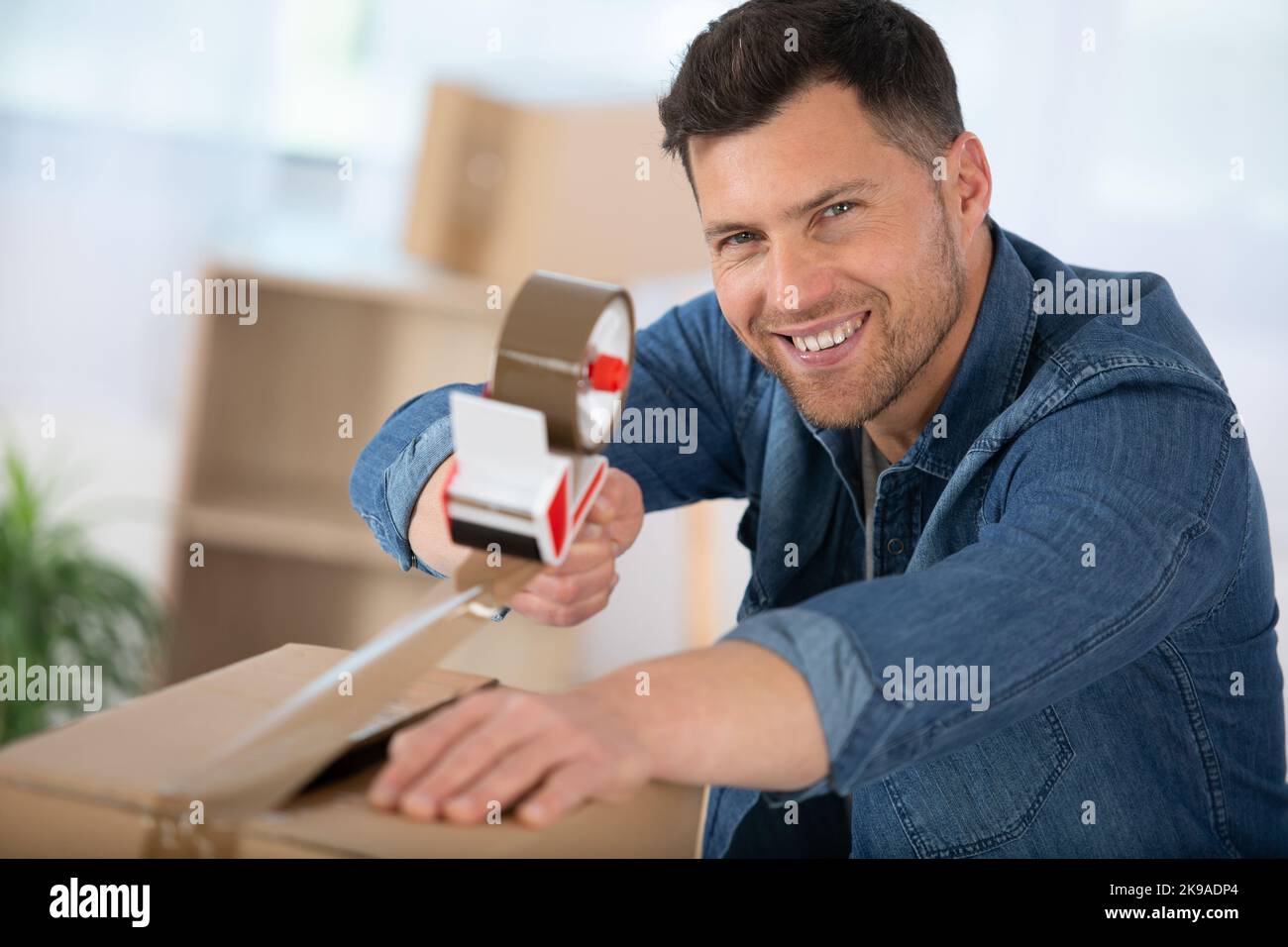 man moving in a new apartment packing and taping boxes Stock Photo - Alamy