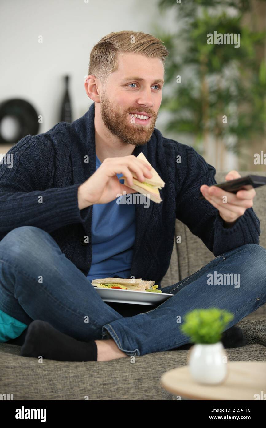 smiling man watching tv while eating sandwich Stock Photo - Alamy