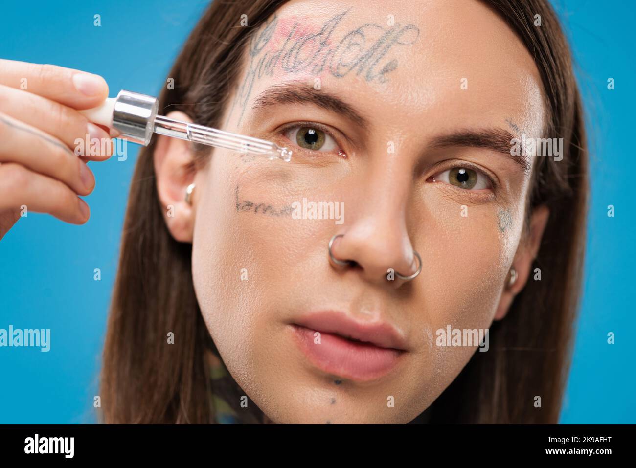 close up of young and tattooed man applying moisturizing serum isolated ...
