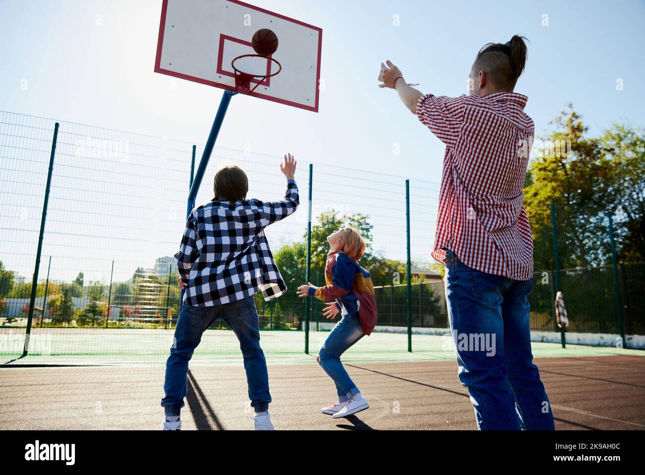 Three teenagers playing streetball with basketball ball at school yard ...