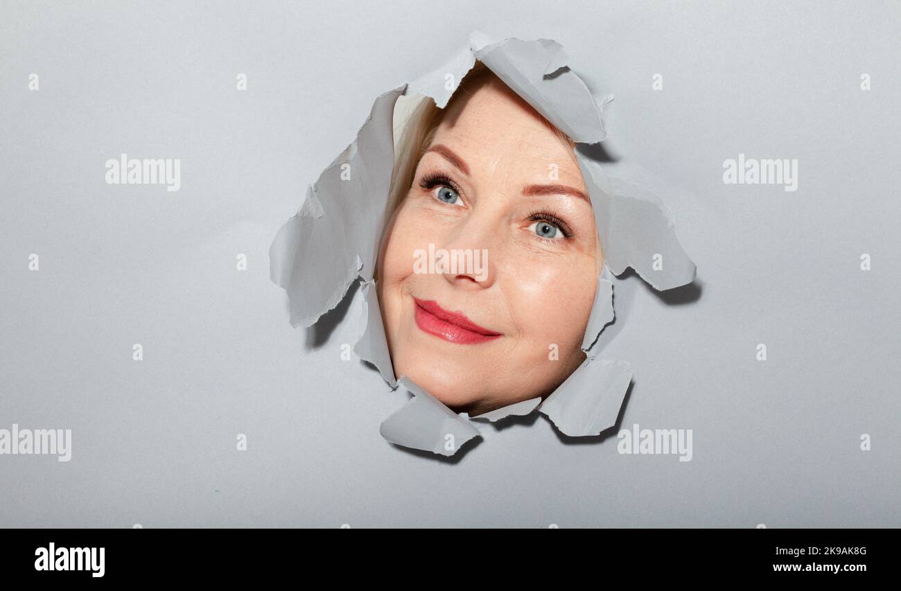 Surprised woman looking playfully in torn paper hole, has excited ...