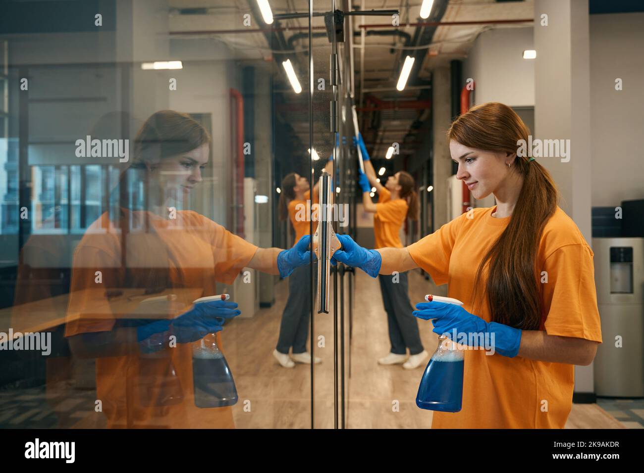 Two young employees cleaning company clean mirrored surfaces coworking ...