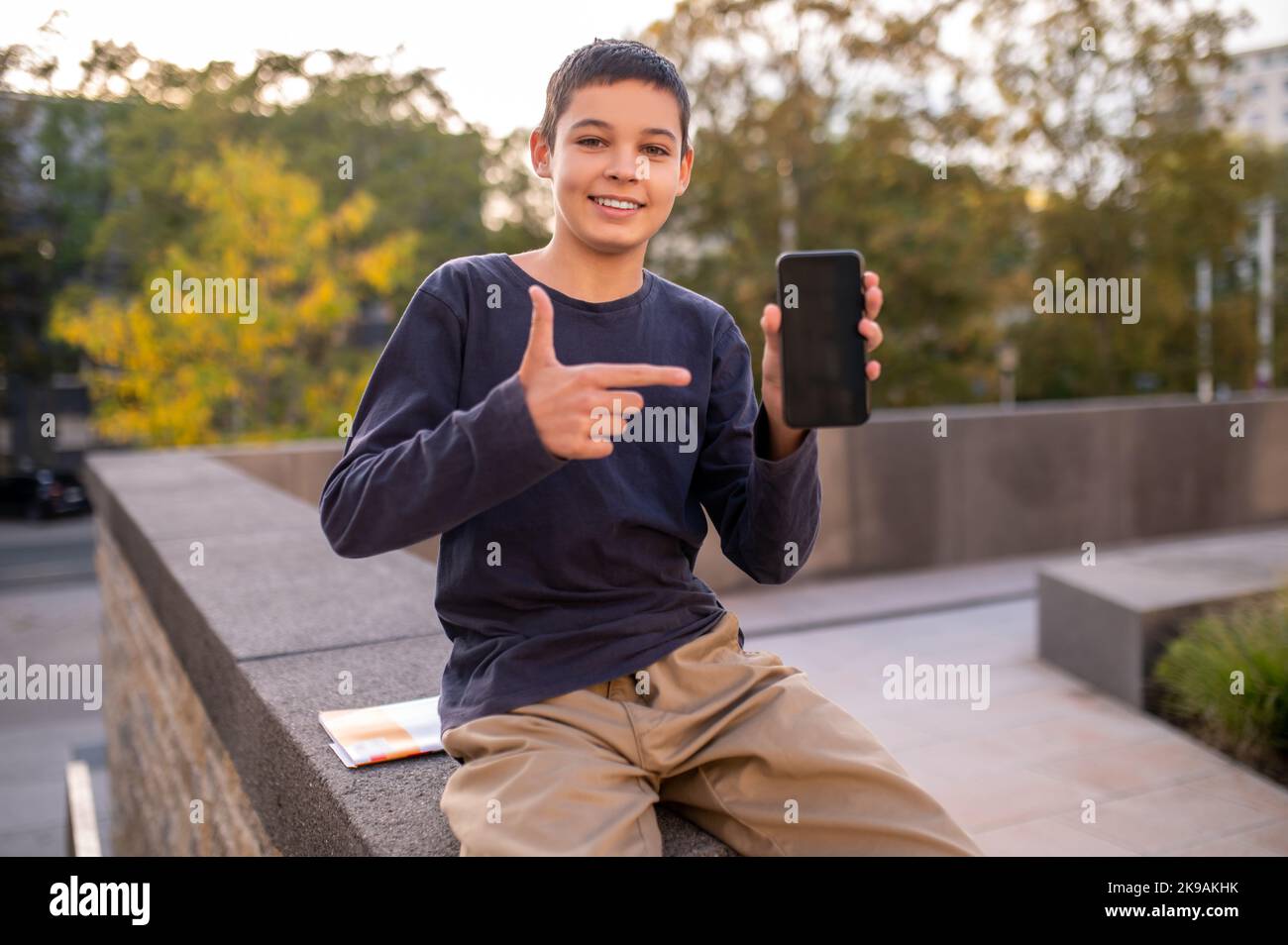 Contented adolescent demonstrating his cellphone before the camera ...