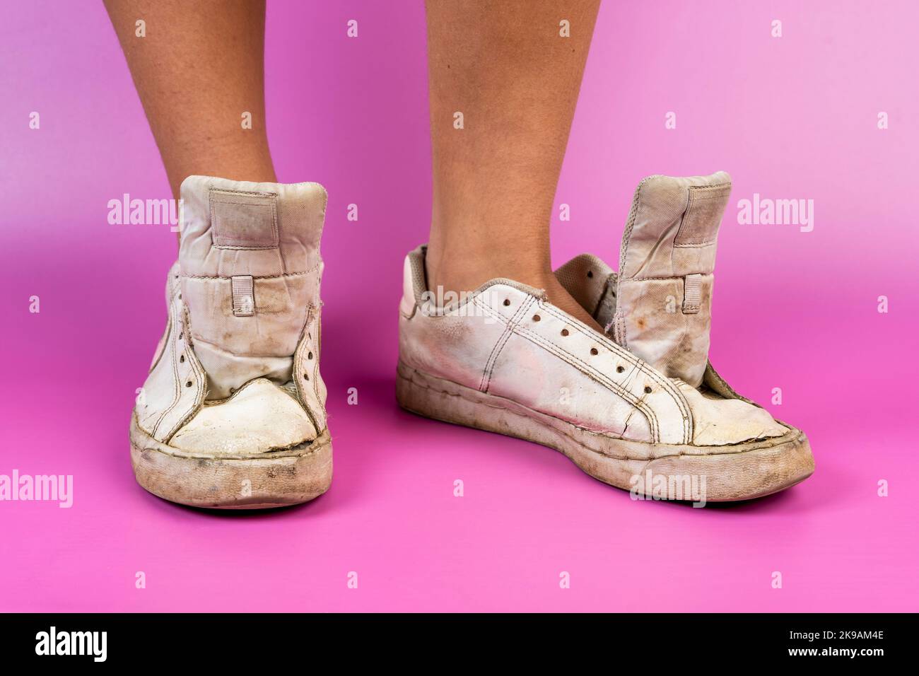 women's legs shod in old battered sneakers on a pink background Stock ...