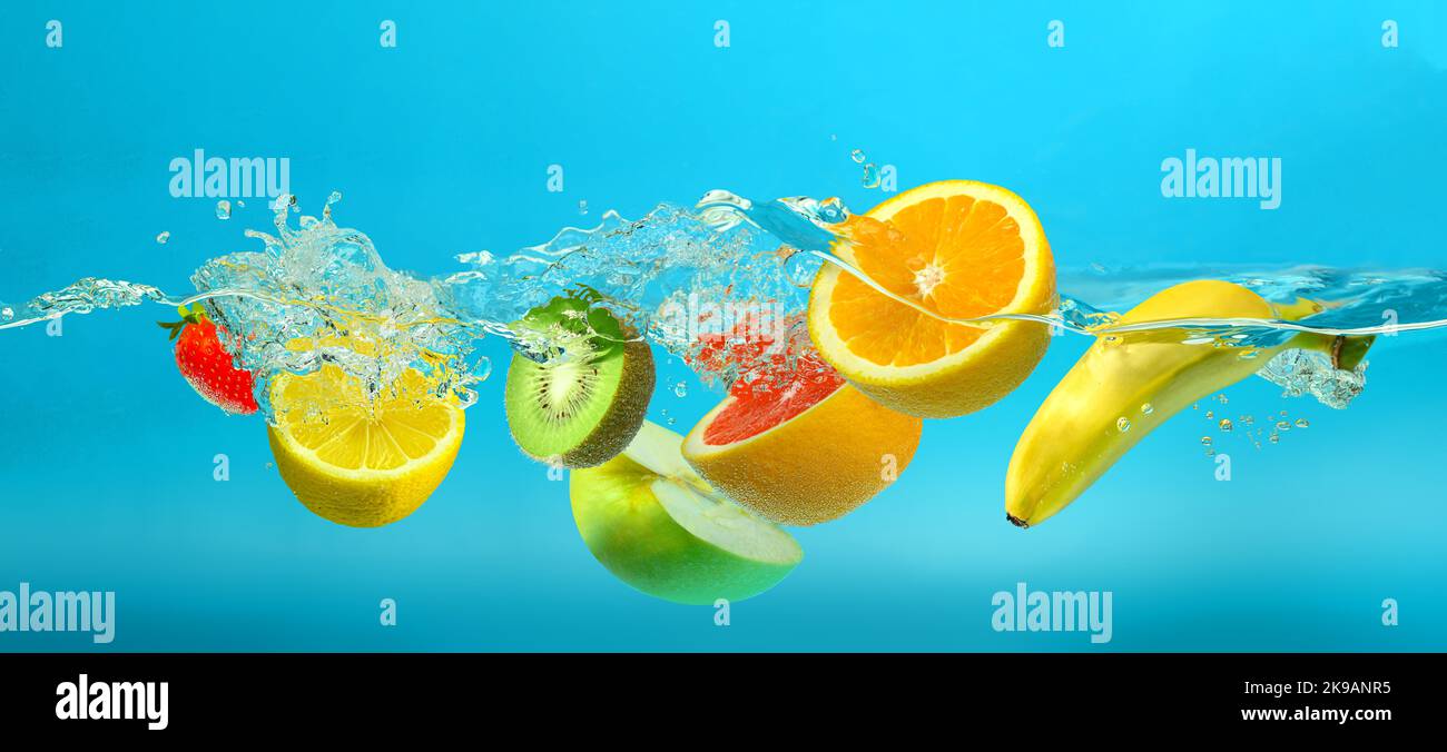 Fruits mix splashing into clear water on turquoise blue background ...