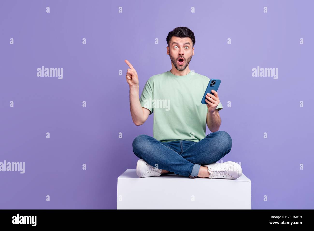 Full body photo of attractive young man sit cube hold device point ...