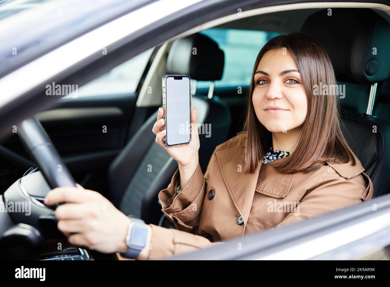 Attractive woman driving a car, she shows blank phone screen and smiles ...
